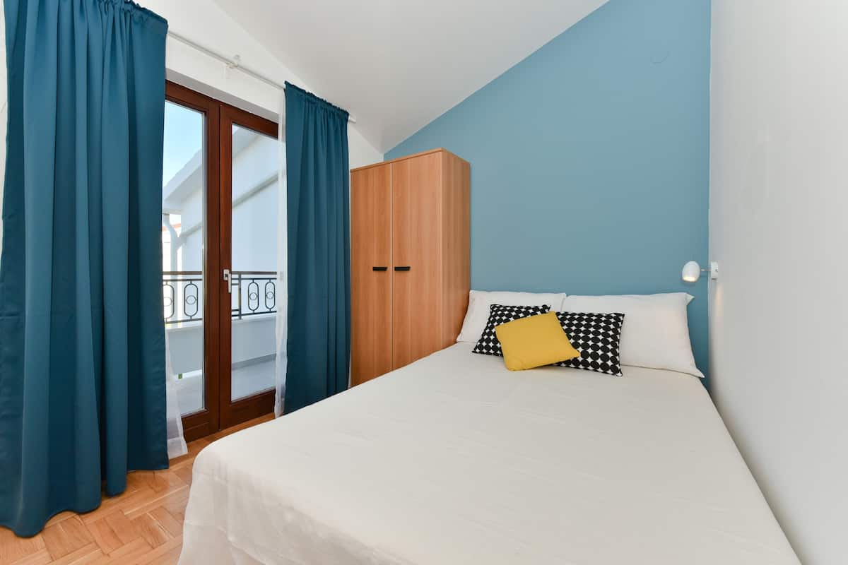 Quarto com cama, guarda-roupa e varanda com cortinas.