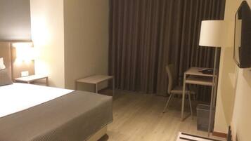 Quarto de hotel com uma cama, uma mesa, uma cadeira, um abajur e uma cortina.