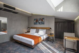 Quarto de hotel moderno com uma cama grande, uma escrivaninha, uma cadeira e obras de arte na parede.