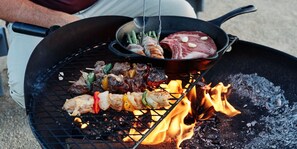 Uma churrasqueira com carnes e legumes variados sendo preparados sobre chamas abertas.