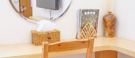 Uma cadeira de madeira, um espelho redondo, uma televisão de tela plana, uma cesta de vime, um livro e um vaso com plantas secas.