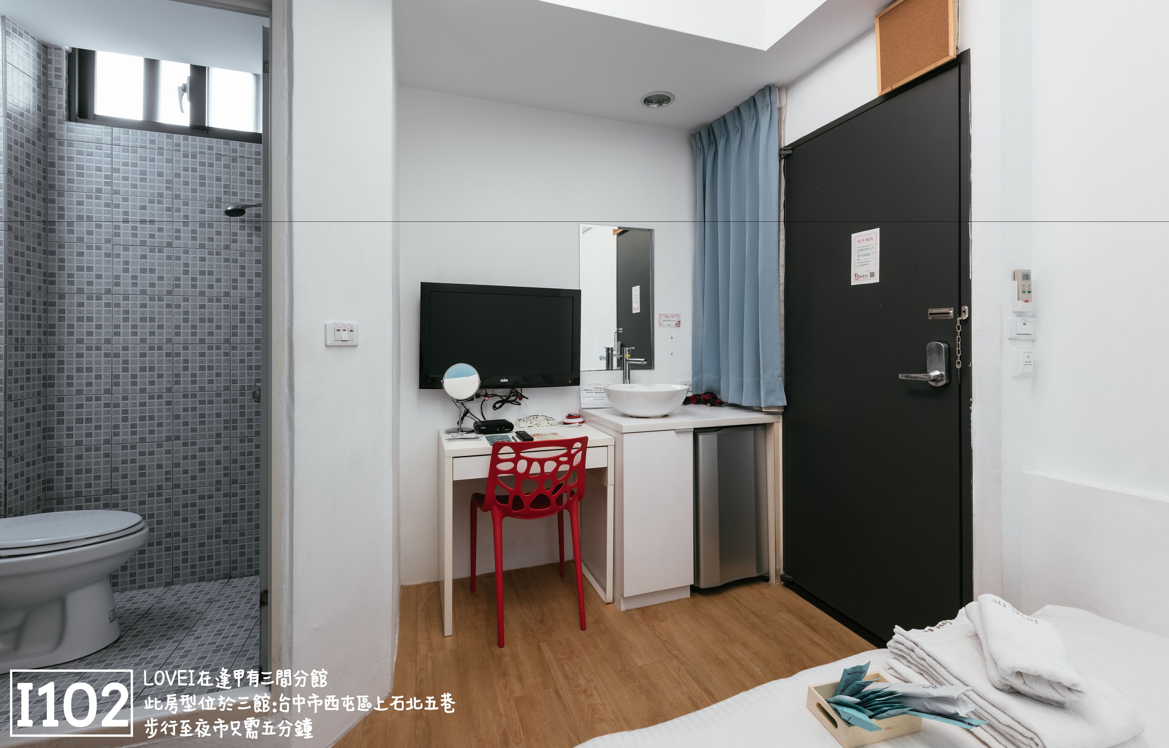Quarto de hotel compacto com sanita, secretária pequena com cadeira, televisão, lavatório e guarda-roupa.