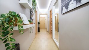 Um corredor estreito com soalho de madeira clara, uma planta à esquerda e um quadro emoldurado à direita.