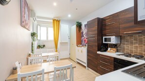 Uma cozinha moderna com armários de madeira, micro-ondas e uma área de refeições com cadeiras brancas e uma mesa de madeira.