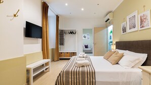 Quarto de hotel moderno com uma cama grande, televisão na parede, um banco e um closet espaçoso.