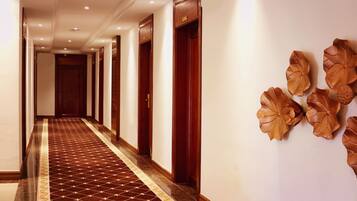 Corredor de hotel com carpete estampado, portas de madeira e um objeto decorativo fixado na parede.
