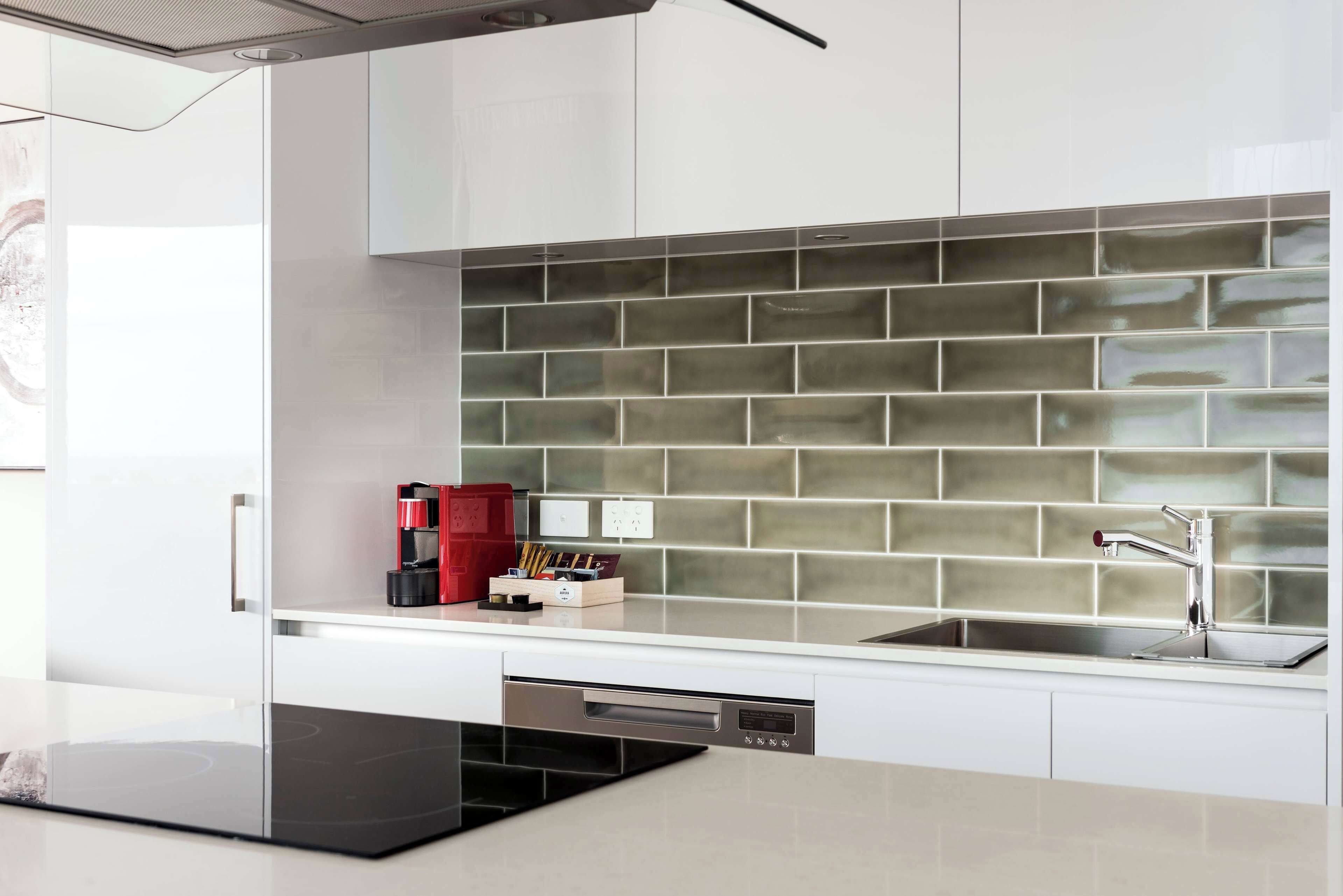 Uma cozinha moderna com um fogão por indução preto e elegante, uma pia de aço inoxidável e um painel atrás do fogão feito de azulejos retangulares.