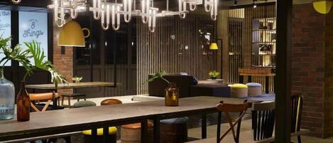Uma sala de jantar moderna com uma mesa comprida, várias cadeiras e luminárias pendentes.