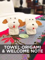 Uma cama com colcha florida, três cães de origami brancos e um bilhete de boas-vindas.