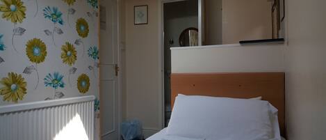Quarto com cama, radiador, porta e parede com padrão floral.