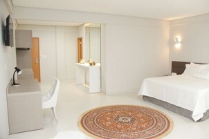 Quarto de hotel moderno com uma cama grande, uma escrivaninha e um banheiro ao fundo.