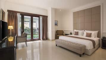 Quarto de hotel com uma cama grande, uma escrivaninha com abajur, uma cadeira e vista pelas portas de vidro.