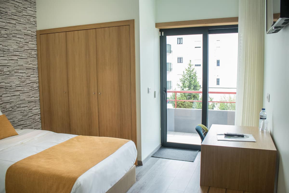 Quarto de hotel com cama, escrivaninha e vista para a varanda externa.