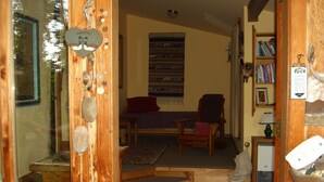 Um quarto aconchegante com uma porta de madeira decorada com pedras e uma placa de boas-vindas, uma mesa pequena, uma cadeira, uma estante de livros e um abajur.