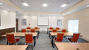 Sala de conferências com tela de projetor, mesas e cadeiras dispostas para reuniões.