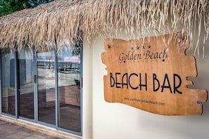 Placa de madeira com os textos 'Golden Beach Park Hotel' e 'BEACH BAR', e um endereço de site.