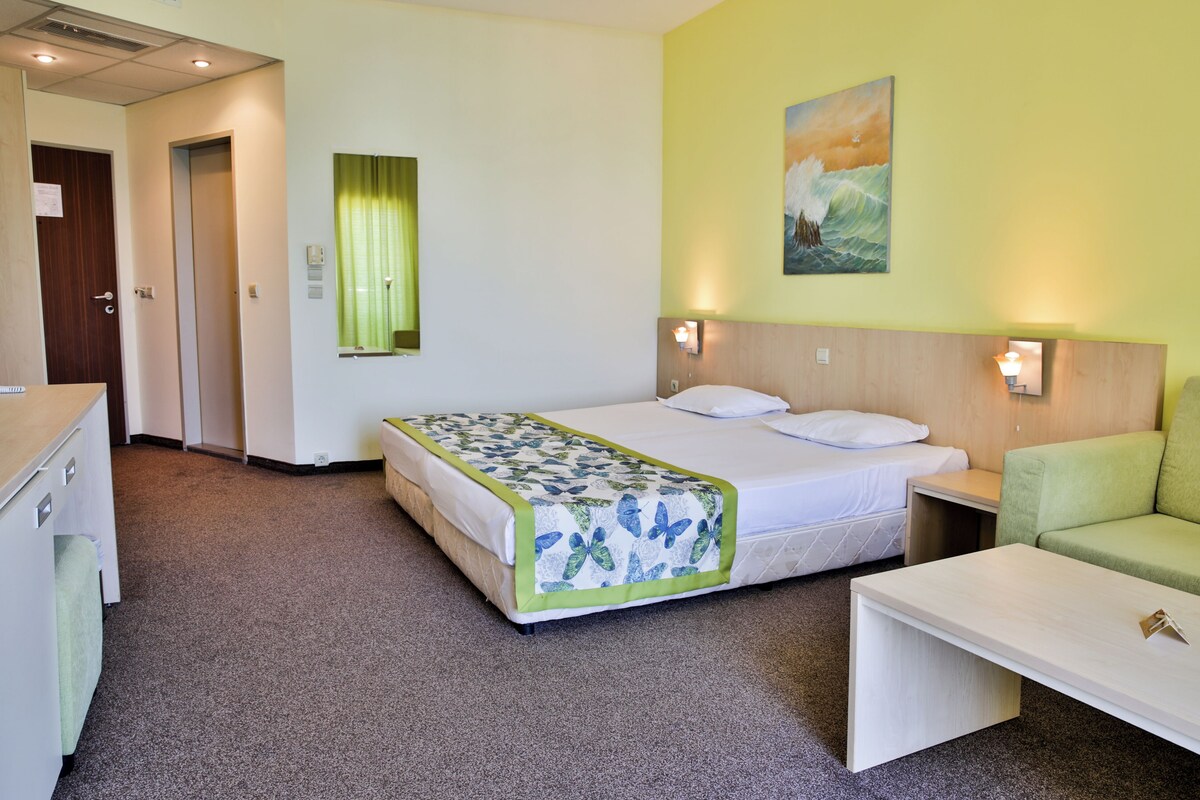 Quarto de hotel com cama, escrivaninha, cadeira, quadro na parede e porta.