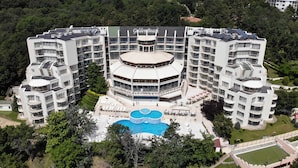 Um hotel com vários andares, um pátio central, piscina e paisagem verde exuberante ao redor.