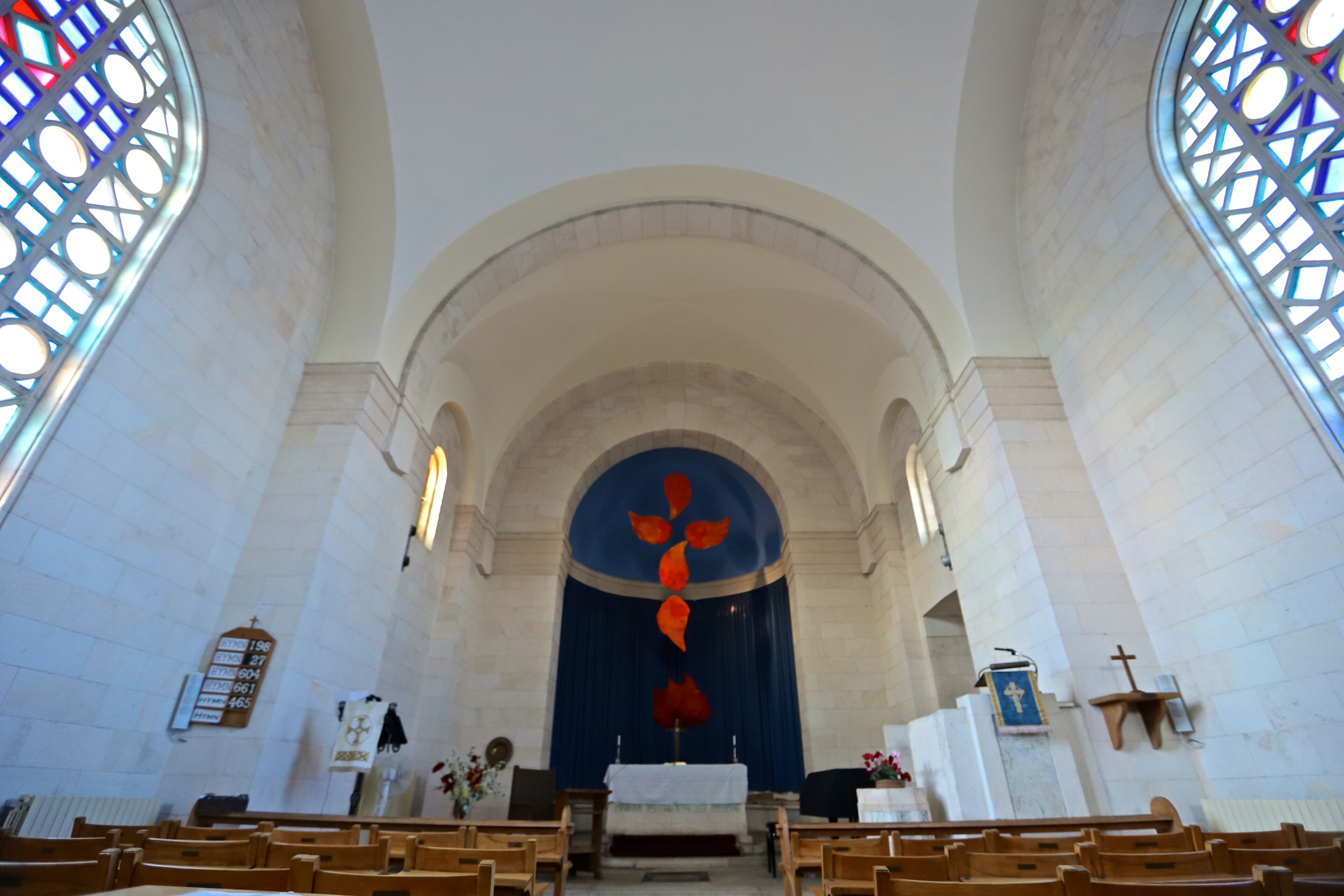 Interior de igreja com tetos abobadados, bancos de madeira, altar central e vitrais.