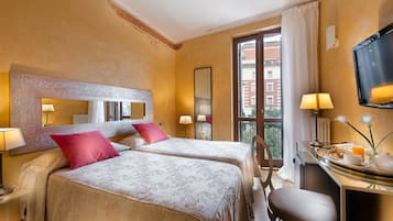 Quarto de hotel com duas camas, uma mesa de trabalho com cadeira, televisão e janela com cortinas.