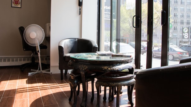 Quarto com mesa de vidro, uma cadeira, um ventilador e vista para a rua.