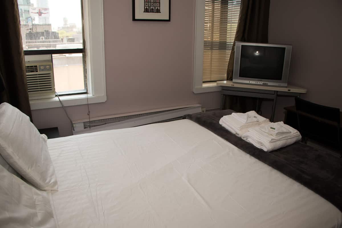 Quarto de hotel com cama, televisão e janela com persianas.