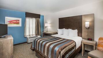 Quarto de hotel com uma cama grande, uma escrivaninha, uma cadeira, uma TV e uma mesa de cabeceira com abajur.