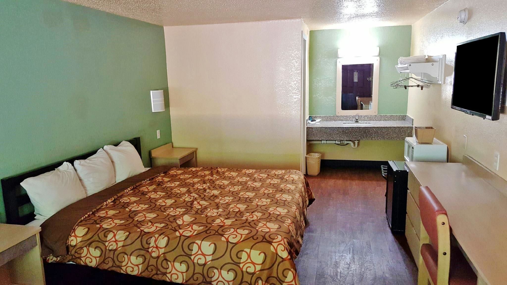 Quarto de hotel com cama, mesa de cabeceira, mesinha, espelho, pia e televisão.