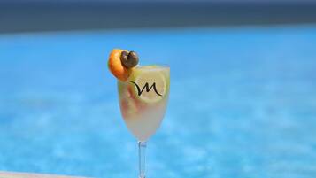 Um copo de cocktail com uma fatia de limão e uma rodela de laranja sobre uma superfície de madeira perto de uma piscina.