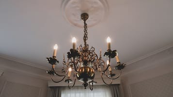 Um candelabro com várias luzes semelhantes a velas, um teto decorativo e uma janela com cortinas.