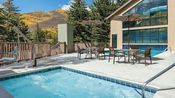 Uma área de piscina com hidromassagem, espreguiçadeiras e uma mesa com cadeiras.