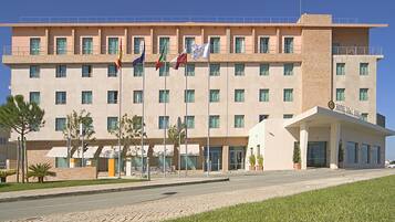 Um hotel de vários andares com telhado plano, várias varandas e entrada central.