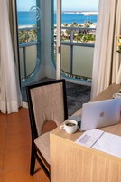 Quarto com vista para a praia, um laptop, uma chávena de café e uma cadeira.