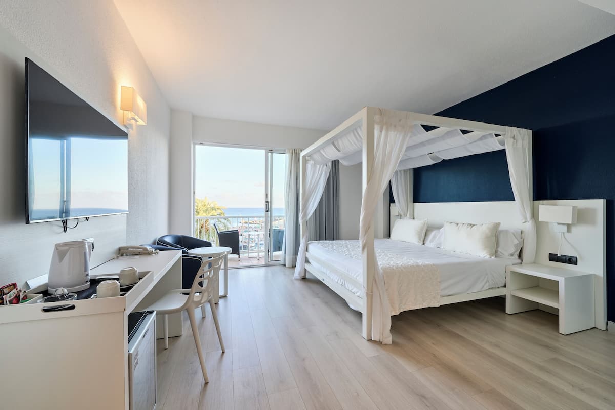 Quarto de hotel moderno com cama, escrivaninha, cadeira e varanda com vista.