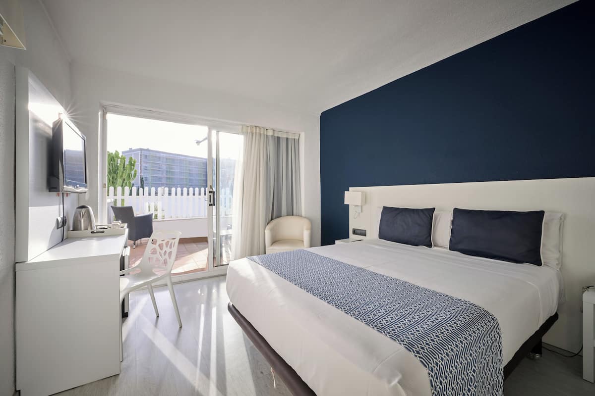 Quarto de hotel com uma cama grande, uma escrivaninha com televisão e uma cadeira.