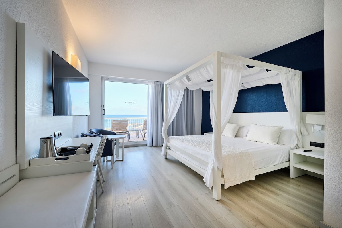 Quarto de hotel moderno com cama de dossel, escrivaninha com cadeira, TV de tela plana e varanda com vista.