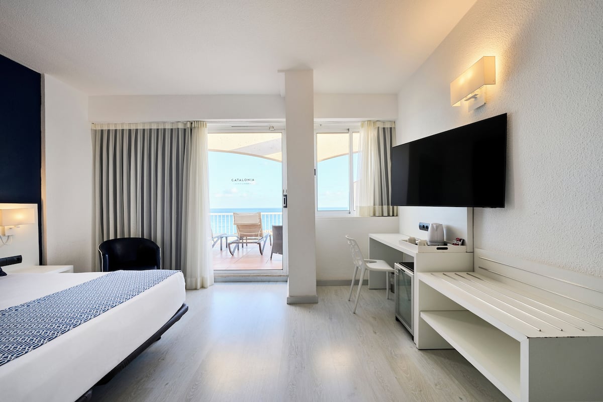 Quarto de hotel com cama, escrivaninha, cadeira, televisão e varanda com vista.