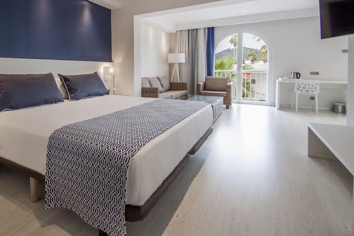 Quarto de hotel moderno com uma cama grande, uma mesa de escritório e uma varanda com vista.