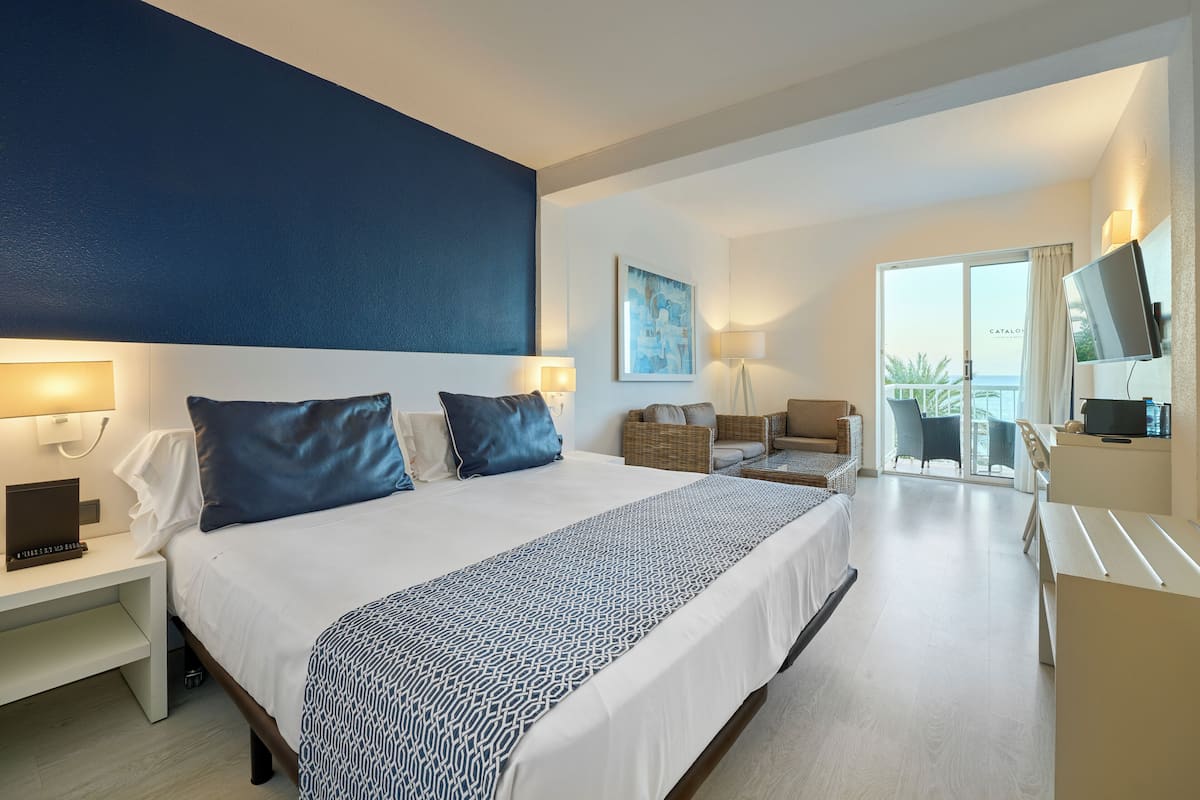 Quarto de hotel moderno com uma cama grande, televisão de tela plana, escrivaninha com cadeira e varanda com vista.