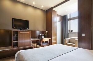 Quarto de hotel com uma cama, uma mesa de trabalho com cadeira, televisão e janela com cortinas.