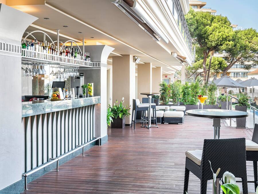 Uma área de bar ao ar livre com um deck de madeira, assentos e vista para a piscina.