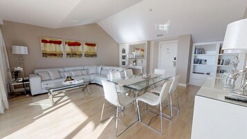 Uma sala de estar moderna com uma mesa de jantar de vidro, móveis brancos e arte abstrata nas paredes.