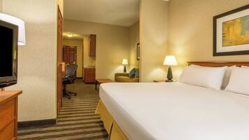 Quarto de hotel com cama, escrivaninha, cadeira, televisão e um quadro na parede.