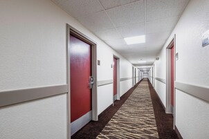 Corredor de hotel com portas, pisos carpetados e teto com iluminação embutida.