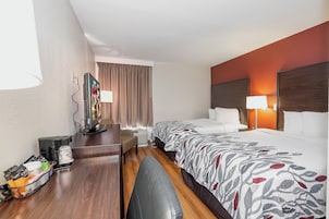 Quarto de hotel com cama, mesa de cabeceira, luminária e escrivaninha com cafeteira.