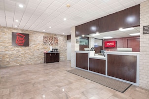 Uma área de recepção com parede de pedra, placa da Red Roof Inn, balcão de check-in e um aviso indicando 'Wi-Fi Gratuito em Todos os Quartos'.