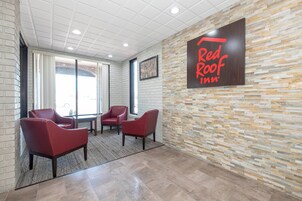 Recepção do Red Roof Inn com parede de pedra, três cadeiras vermelhas e uma placa grande.
