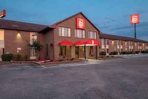 Um Red Roof Inn com fachada de tijolos, várias janelas e um estacionamento à frente.