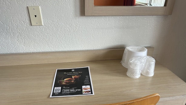 Mesa de quarto de hotel com um menu de serviço de quarto, uma cadeira e uma janela com vista para uma varanda.