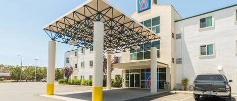 Um hotel com entrada coberta, um logotipo azul e área de estacionamento.